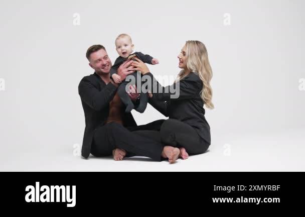 Mother and father wearing black clothes sit on the floor in studio ...