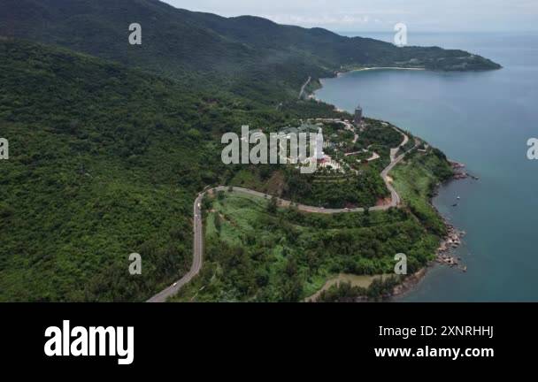 A scenic road cuts through a vibrant green forest beside a tranquil ...