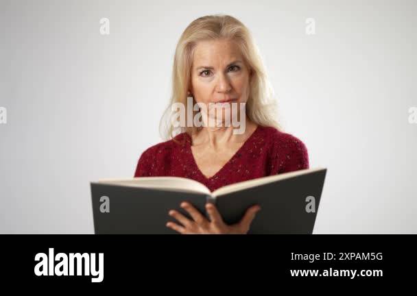Reading then looking into camera, happy pretty elderly blond woman 50s ...