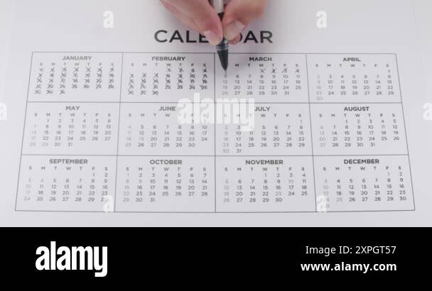 Close-up of a hand marking days on a 12-month calendar with a pen ...