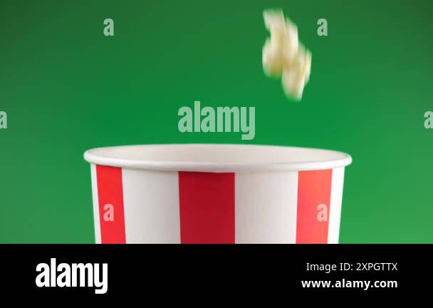 Popcorn grains falling into red and white striped bucket isolated on ...