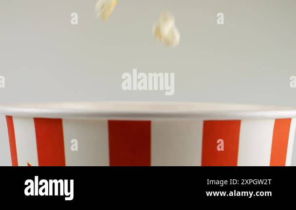 Popcorn grains falling into red and white striped bucket isolated on ...