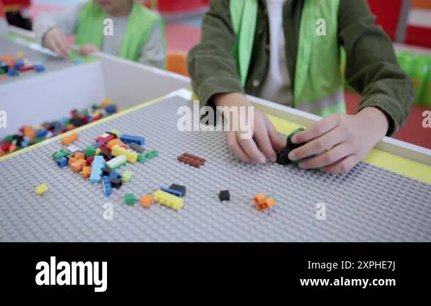 Two kids playing and building with colorful plastic bricks on the table, wearing waistcoat in ...