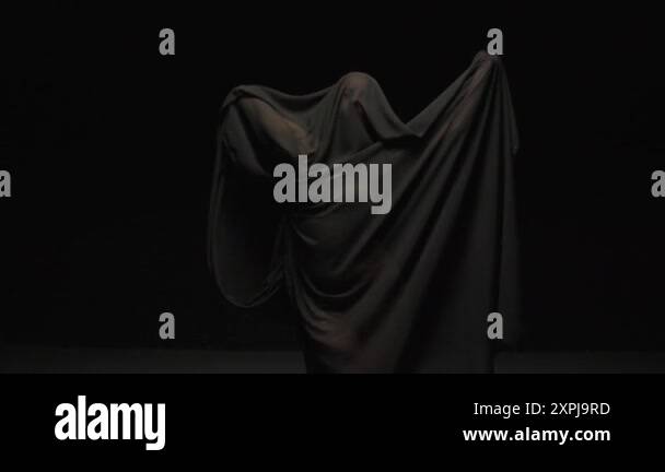 An enigmatic figure elegantly draped in rich black fabric, creating a captivating and mysterious ...