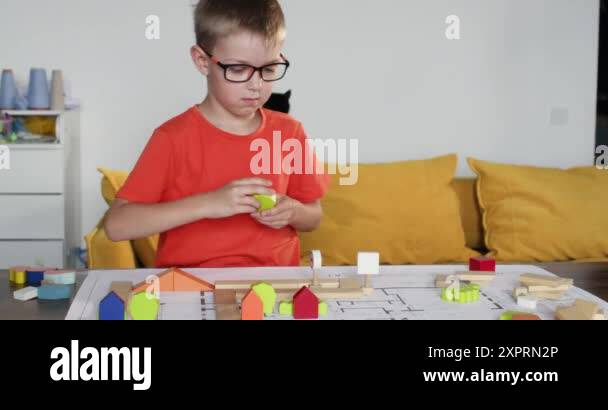 Smart boy with glasses builds town of wooden details on blueprints at ...