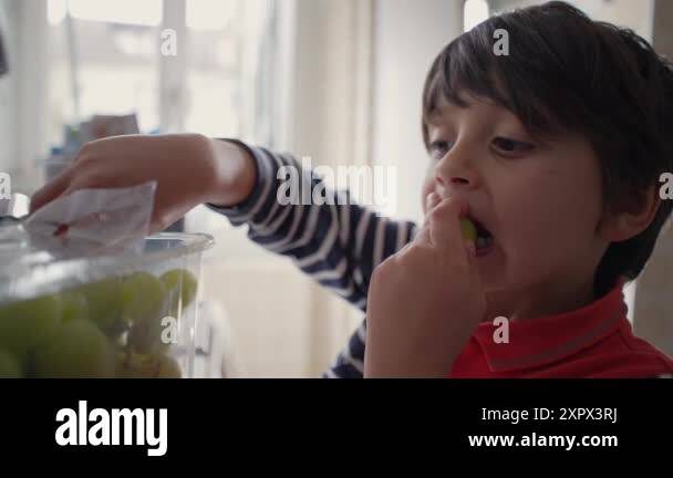 Young boy reaching into a container of green grapes, showing his ...