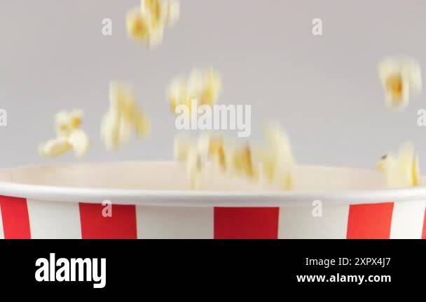 Popcorn grains falling into red and white striped bucket isolated on ...