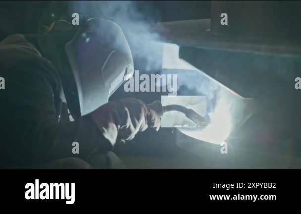 Welder welds metal structures at factory. Stock clip. Masked welder is working on assembly of ...