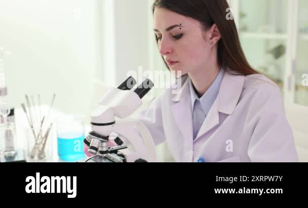 Researcher examines sample using modern microscope in lab. Scientist makes precise adjustments ...