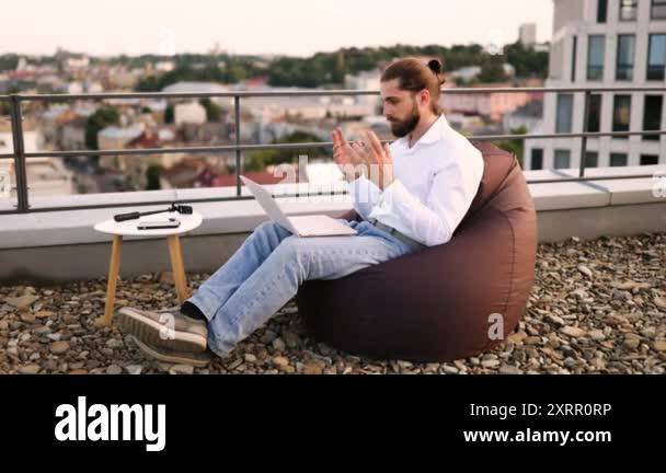 Man working remotely on rooftop while engaging in video call on laptop ...