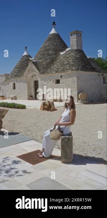 Young hispanic woman sitting outdoors in alberobello, italy, in front ...
