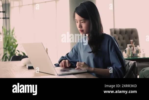 Young Asian woman sit at desk in modern workspace typing text on laptop keyboard, review and ...