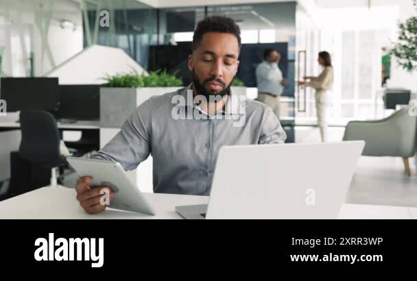 Male office employee holding digital tablet using laptop sit at ...