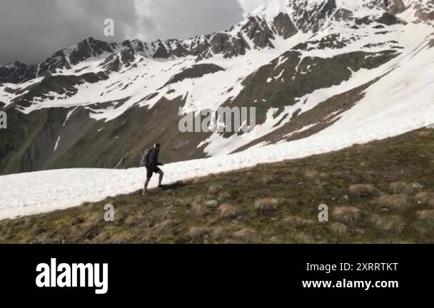 Aerial of solo alpinist climbs snowy mountains, carries backpack ...