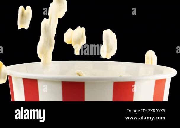 Popcorn grains falling into red and white striped bucket. Movie snack ...