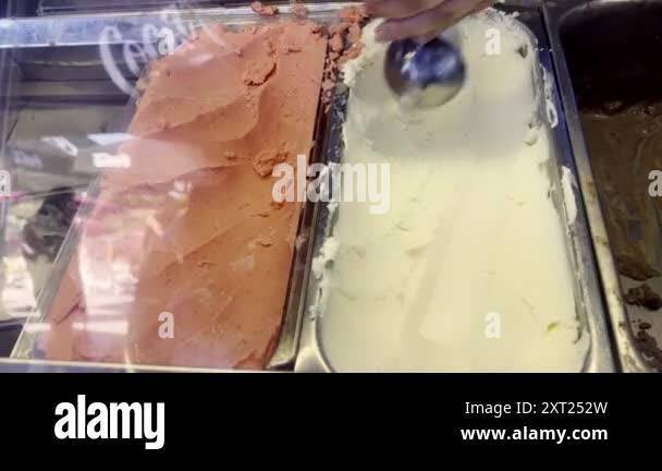 Hand scooping ice cream from a container at a gelateria. Various ...