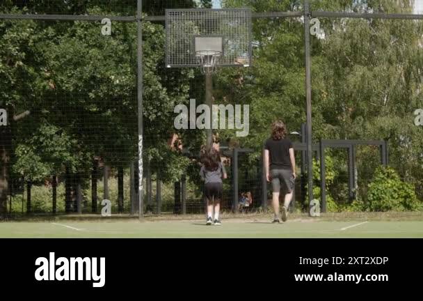 Two brothers on a basketball court make shots at the hoop. The ball ...
