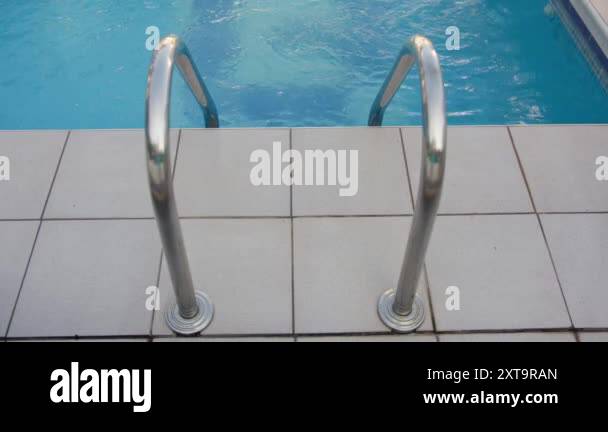 Stainless steel ladder leading into a clear blue swimming pool. Focuses ...