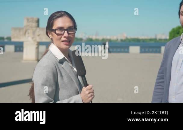 Along the bustling city waterfront, a TV reporter interviews a male ...