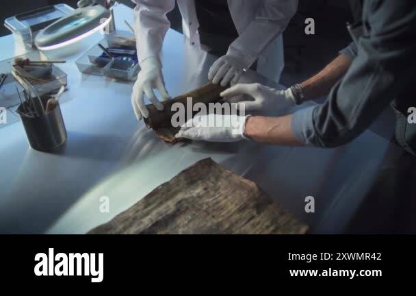 Two archaeologists in gloves carefully open ancient Egyptian papyrus on ...