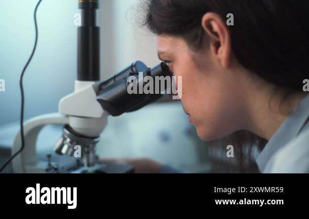 Close up of young scientist using microscope, analyzing sample in archaeological or medical ...