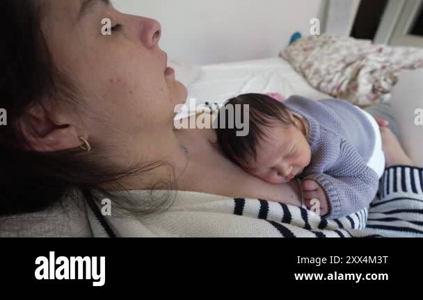 Mother resting on a bed with her newborn sleeping peacefully on her ...