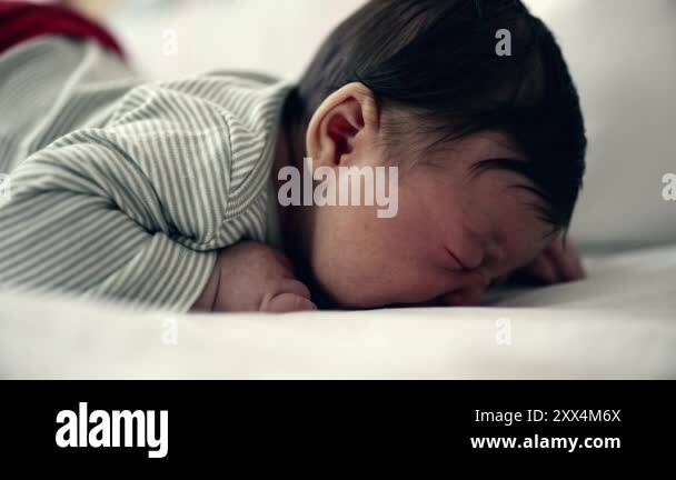 Newborn baby crying on a bed, with a pained expression and tightly shut ...