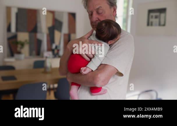 Senior man lovingly holding his sleeping infant grandchild, embracing the baby gently in a ...