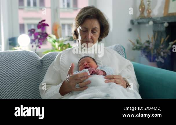 Grandmother sitting with newborn on her lap, cradling the baby gently ...