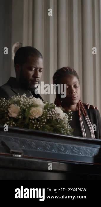 Vertical view of two African American relatives standing at coffin ...