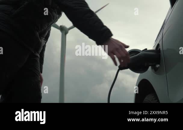 Male hands disconnect wind charging station power connector from EV car ...