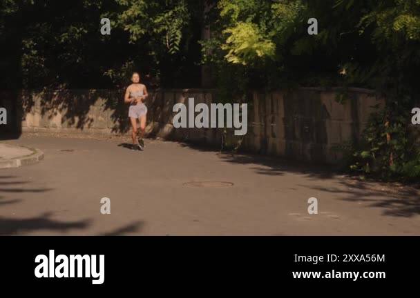 A young woman goes for a run on a sunny day in the city. She is wearing ...