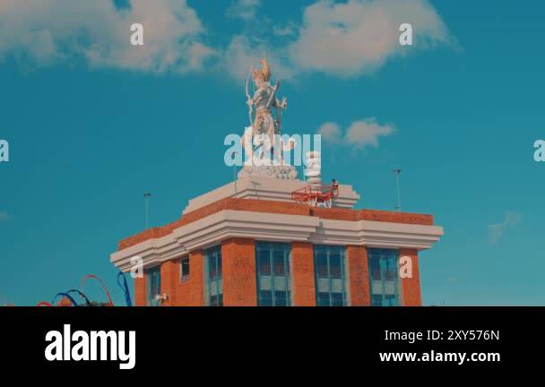 A large white statue of a deity stands atop a red brick building ...