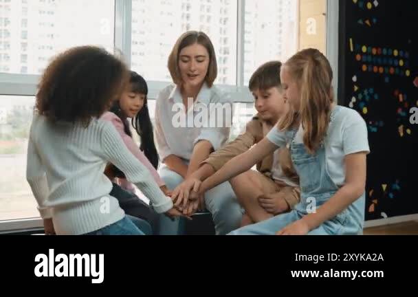 Teacher and diverse students putting hands together at classroom. Young ...