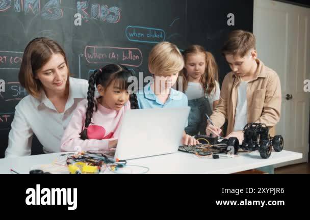 Diverse student writing engineering code while boy fixing mother board. Teacher giving advice ...