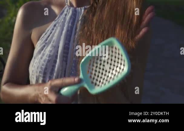 A close-up of a girl standing outdoors as she combs her hair. The ...