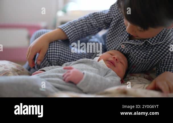 Older brother interacting gently with newborn sibling, both lying on a ...