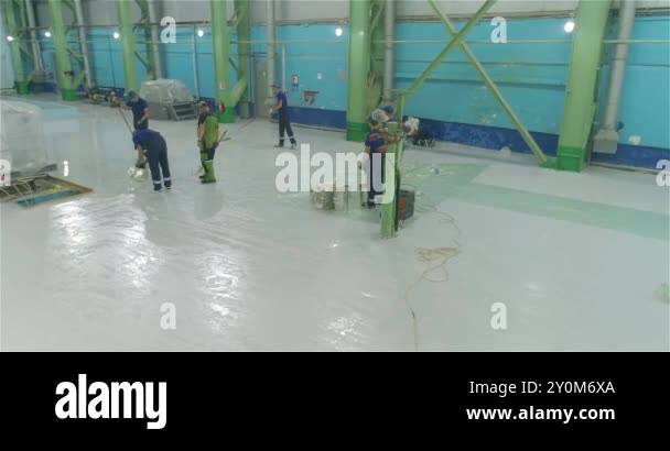 Builders apply a polymer coating to the floor of an industrial building ...