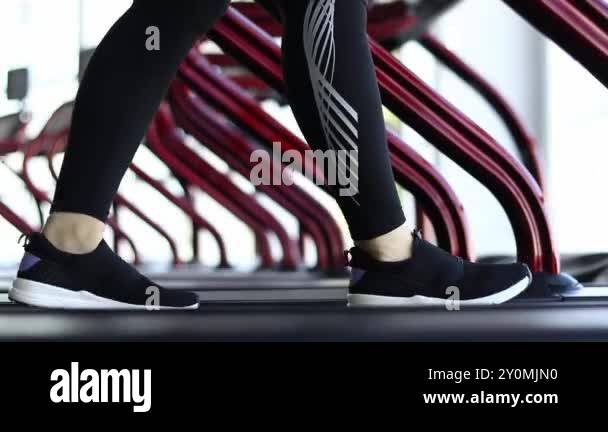 Treadmill in the gym. Side view of legs in sneakers walking on the ...