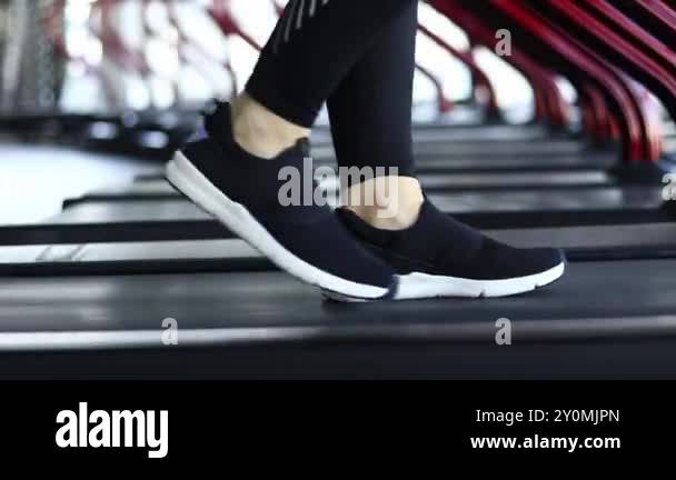 Treadmill in the gym. Side view of legs in sneakers walking on the ...