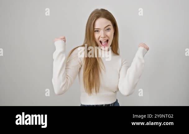 Excited young blonde woman in sweater, arms raised, screaming in joy ...