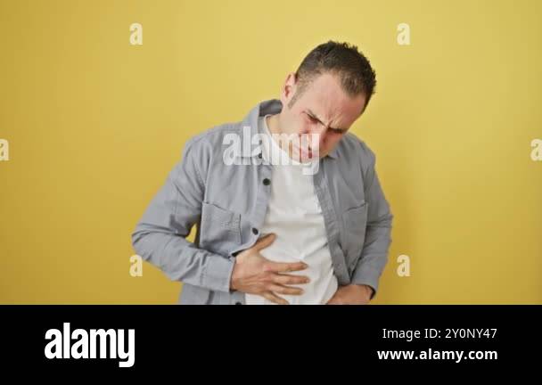 Attractive young hispanic man in pain, clutching stomach with a grimace ...