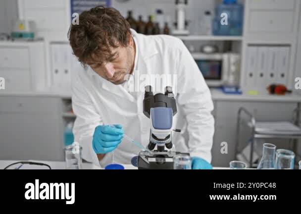 A focused man in lab coat uses microscope in a well-equipped laboratory ...
