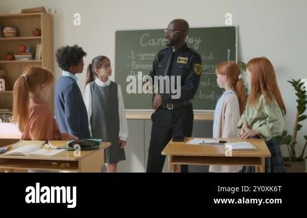 Medium full shot of young black policeman in uniform standing classroom ...