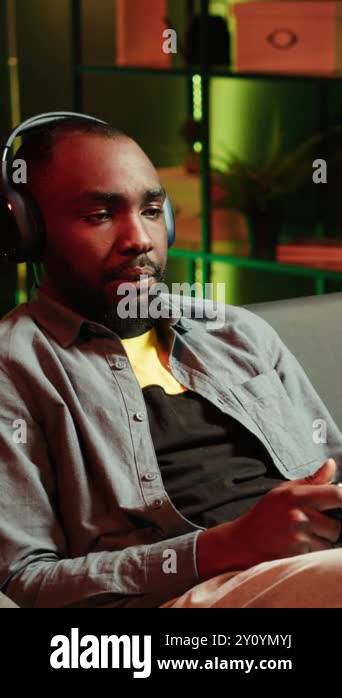 Vertical video Tired gamer in RGB lit home late at night gaming with ...