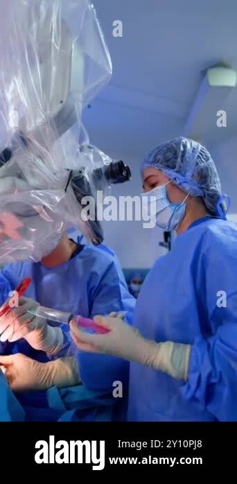 Assisting female doctor holds the syringe and looks into microscope ...