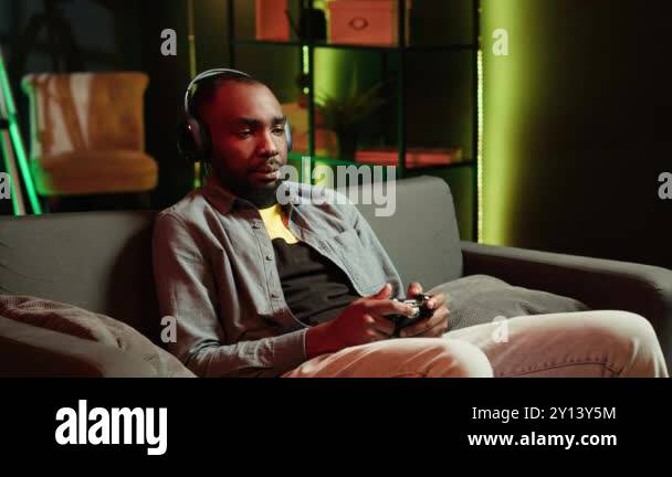 Tired gamer in RGB lit home late at night gaming with gamepad. Man ...