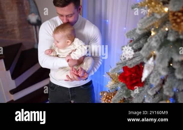 Caucasian man wearing warm white sweater holding a baby in light ...