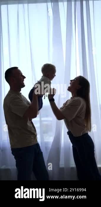 Mom and dad stand at the window with their beloved baby. Loving parents ...