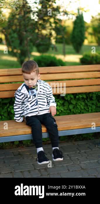 Beautiful little kid sitting on the bench outdoors. Smiling baby ...